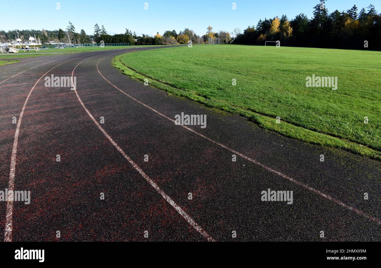 An old, worn and overgrown with grass running track in a school field ...