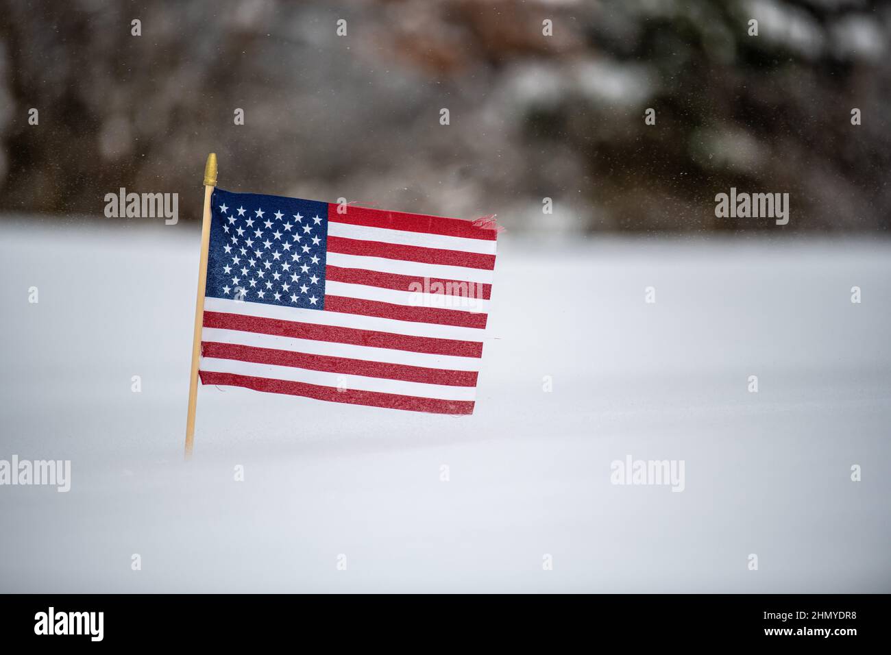 Closeup of a small US flag in the snow in a field with a blurry ...