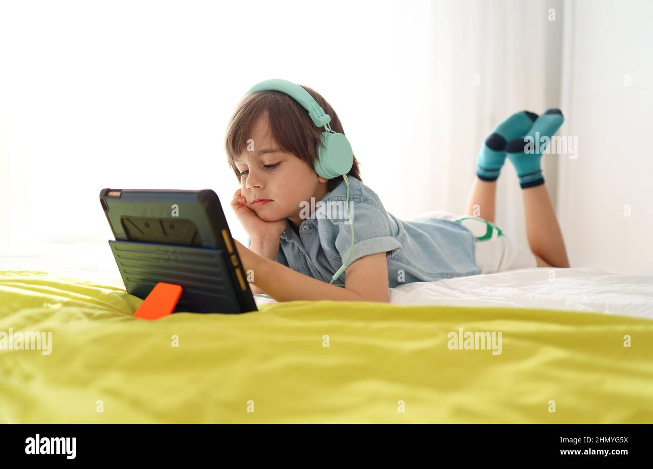 Bored little boy looking at tablet with sad face lying down on sofa ...