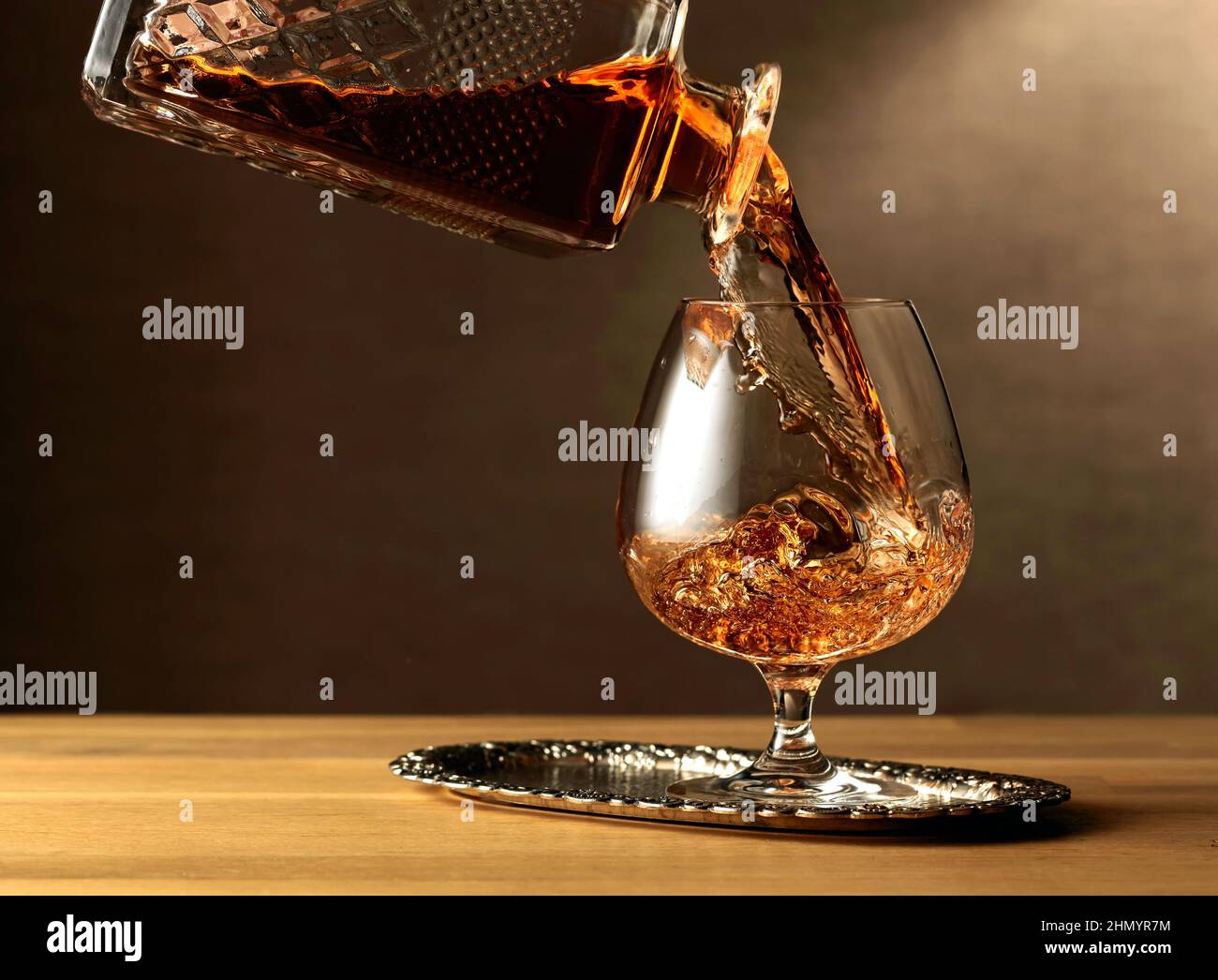 Brandy is poured from a decanter into a snifter glass. Cognac on an oak ...