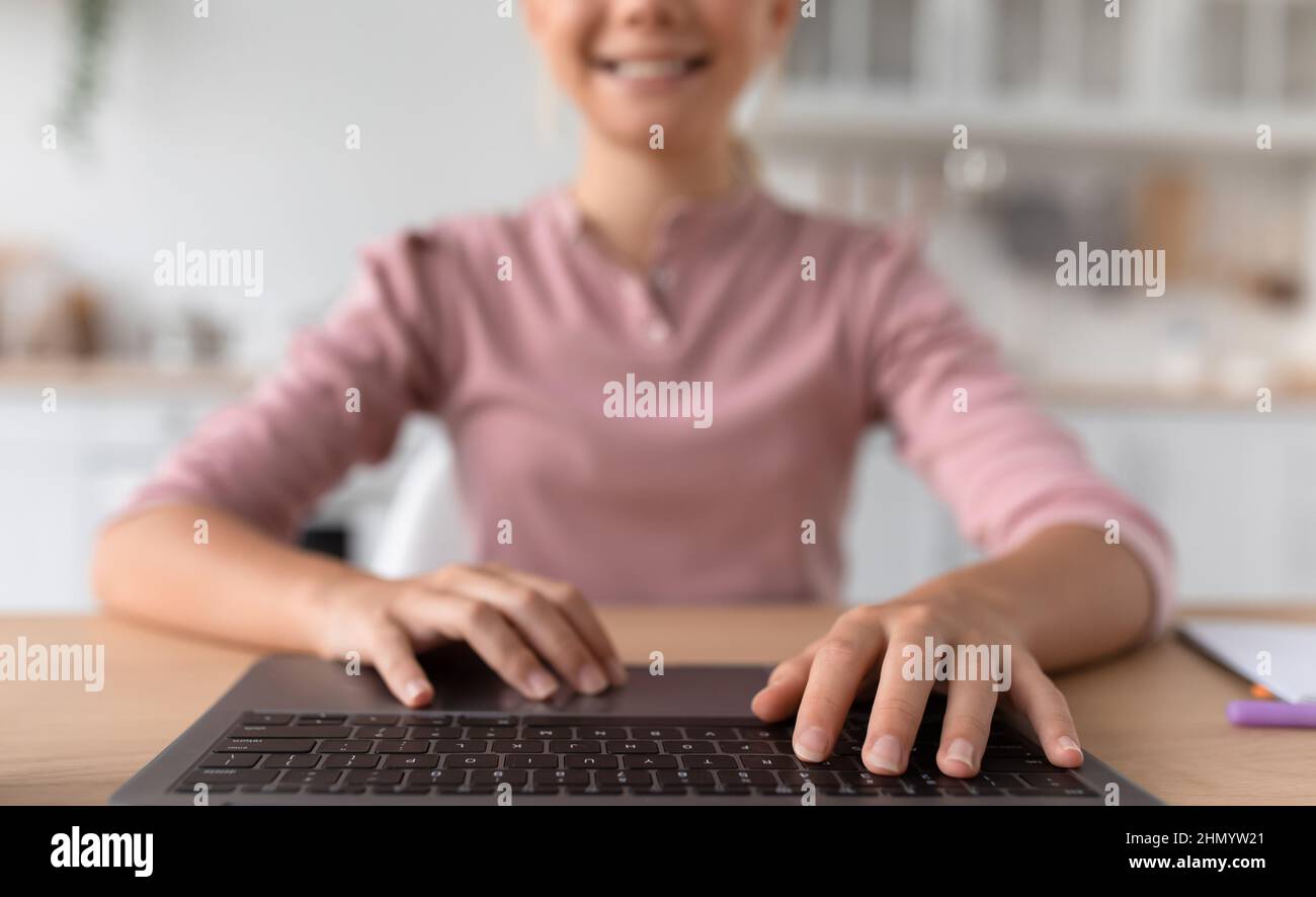 Glad cute european teenage girl typing on laptop keyboard in kitchen ...