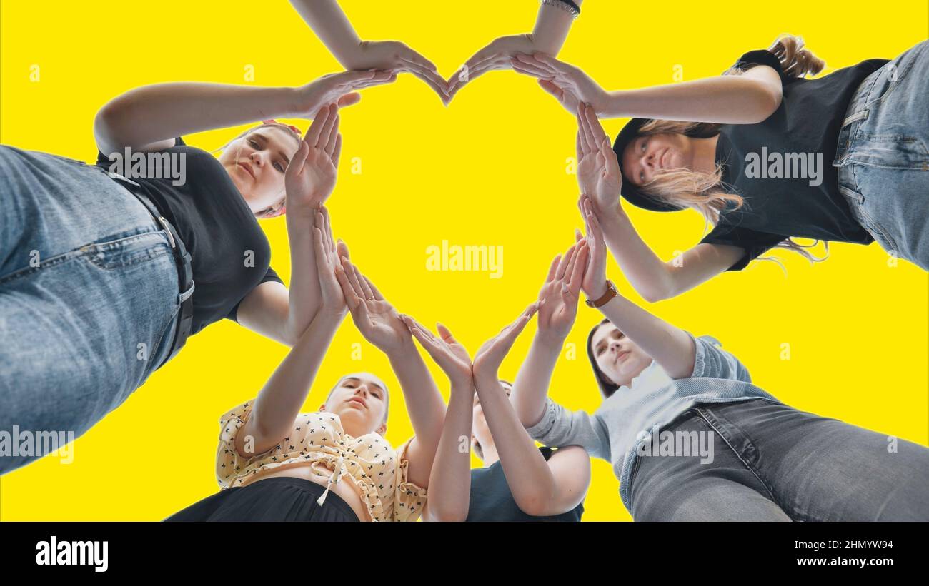 Female friends make a heart shape from their hands on a yellow ...