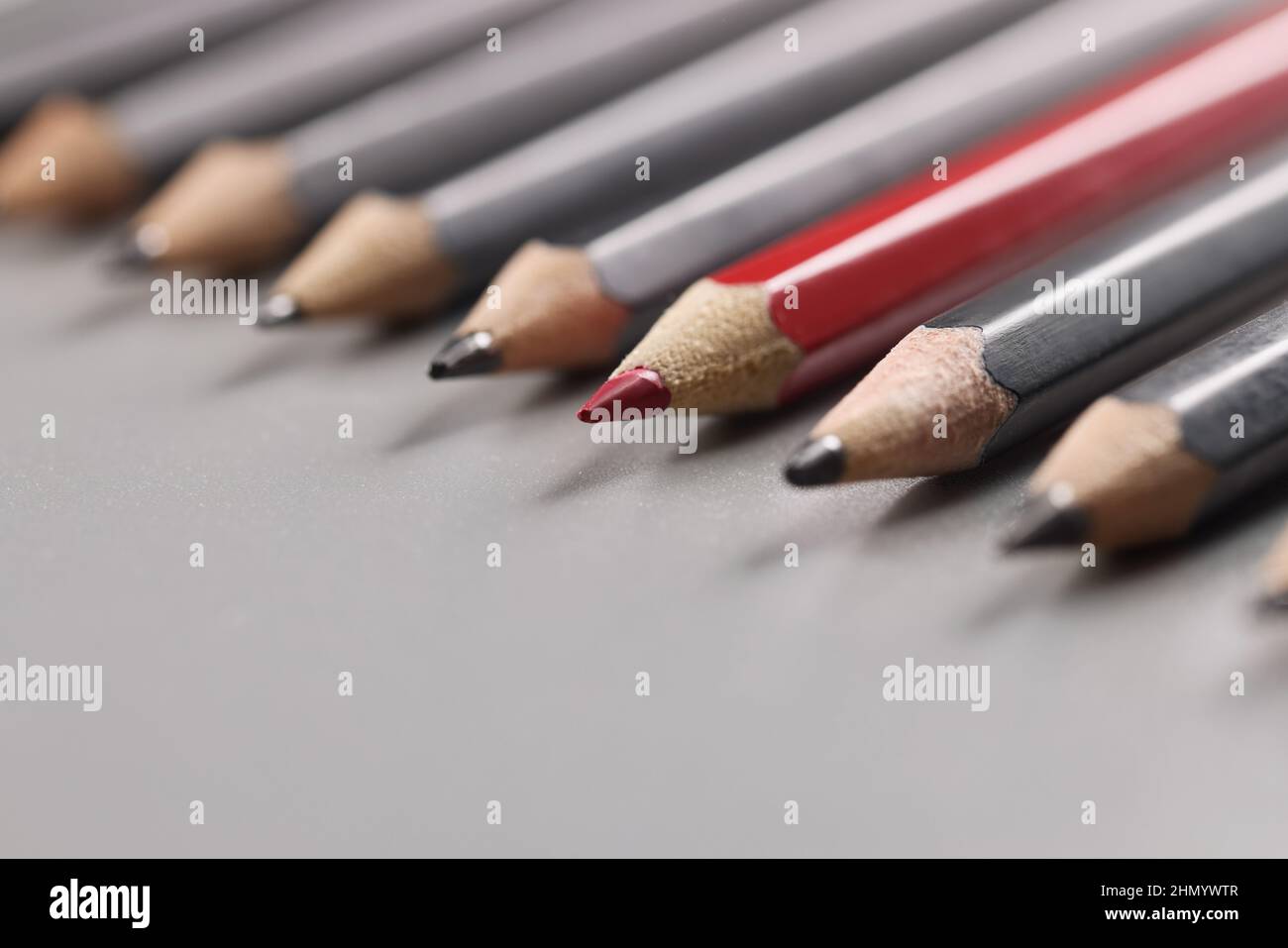 Pencils tips put on grey surface in strict order, red one among black ...
