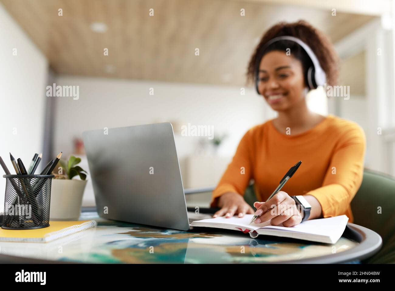 Black woman sitting at desk, using computer writing in notebook Stock ...