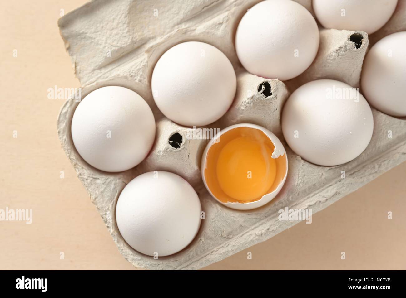 White eggs in a box, one with open shell showing the yellow egg yolk ...