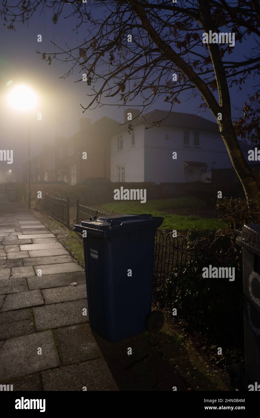 Wheelie bin under street lights on a wet foggy morning in North London ...