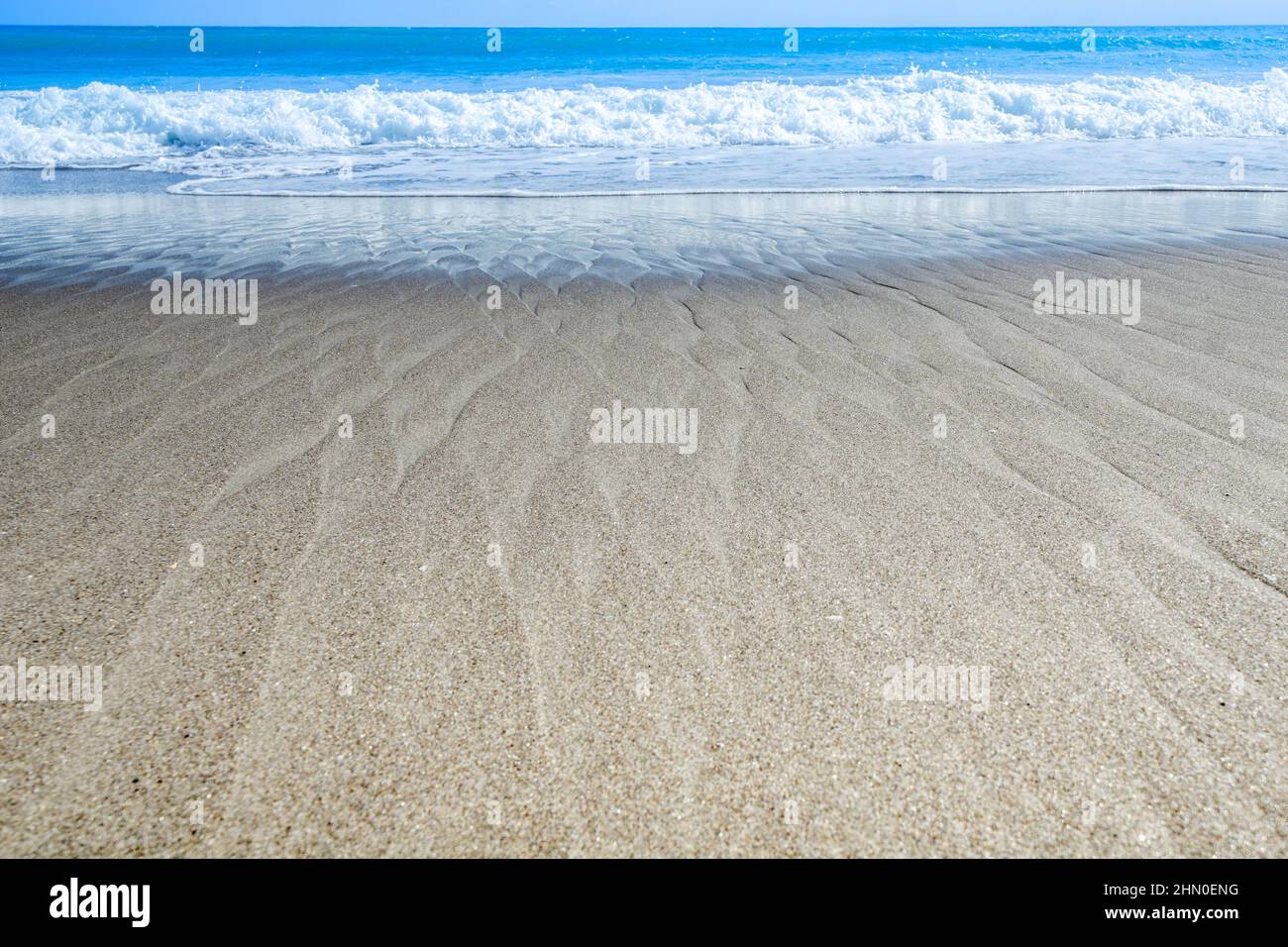 Sandy beachfront at Pikowai with patterns left in sand as water recedes ...