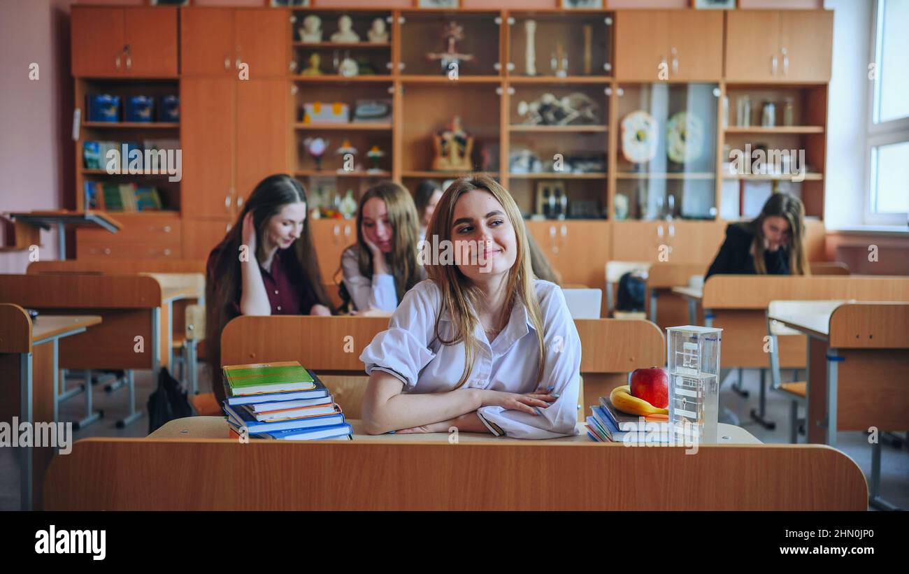 A girl student sitting at a desk raises her hand in the class Stock ...