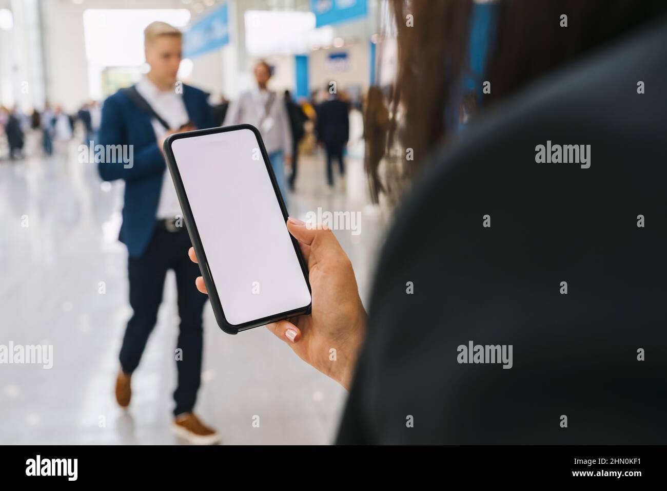 view of a smartphone in female hands with empty screen, with crowd of ...