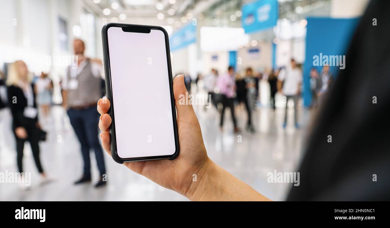 Businesswoman hand holding black cellphone with white screen at a trade ...