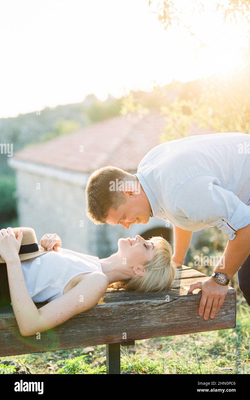 Smiling man bent over woman lying on wooden bench Stock Photo - Alamy