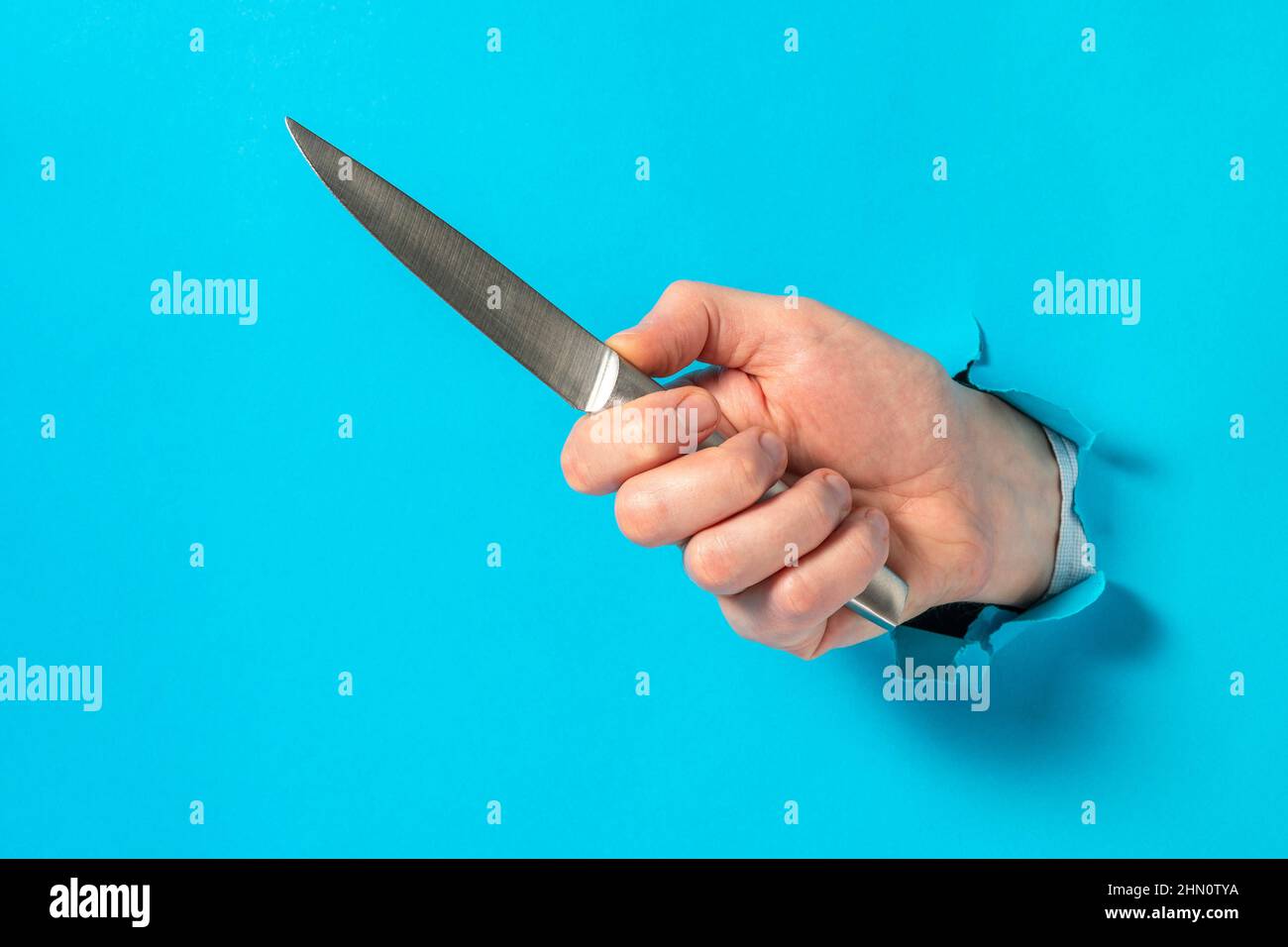 Hand holding knife in hole of blue paper. The concept of aggression ...