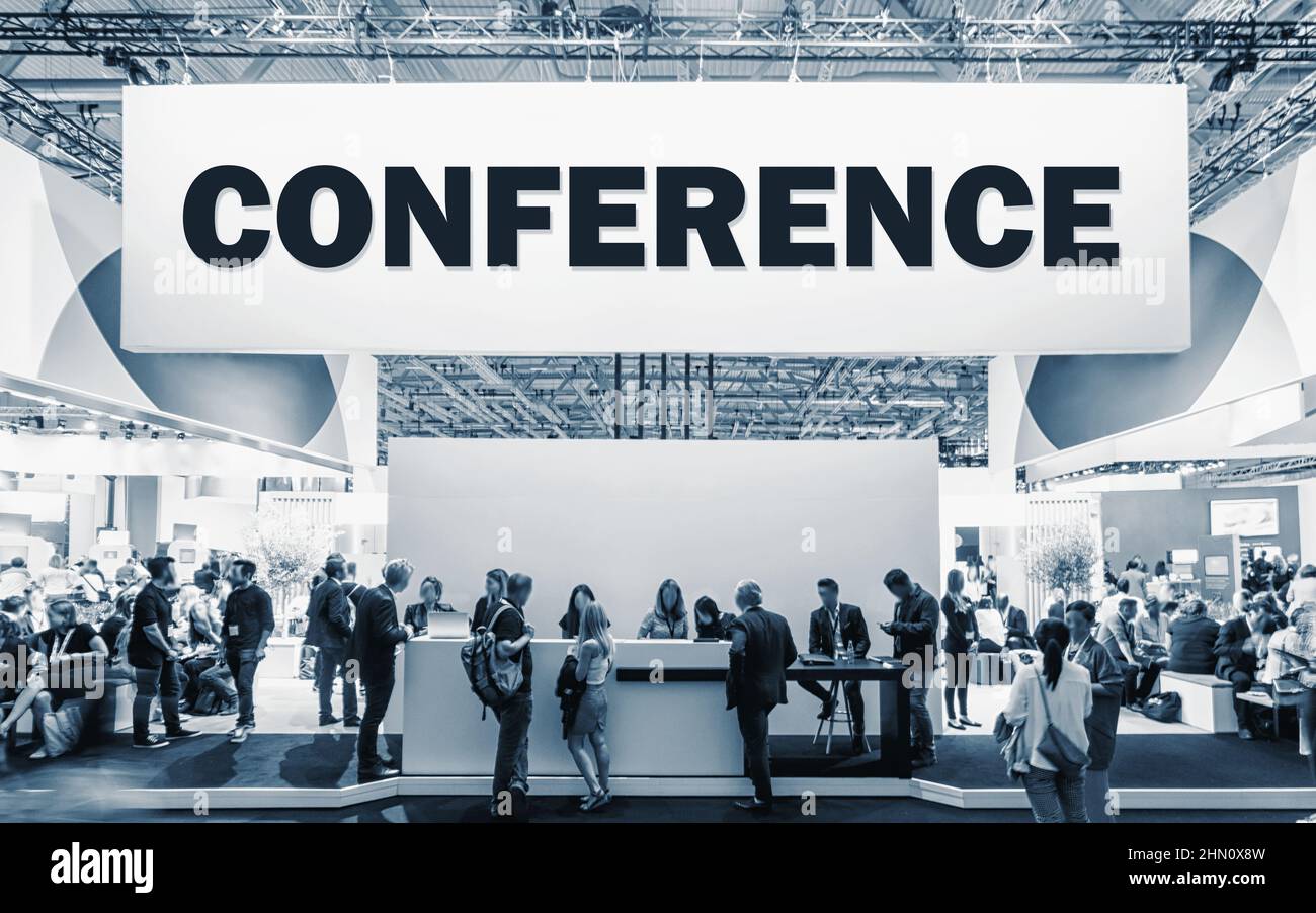 Crowd of people at a trade show booth with a banner and the text ...