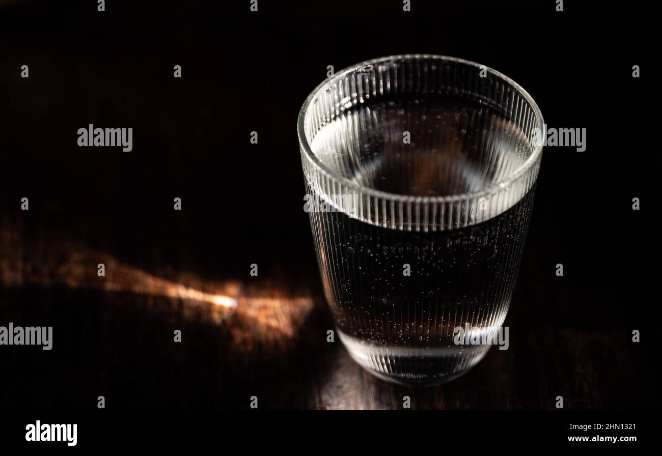 A glass of water lit by the sun in dark background. Selective focus on ...