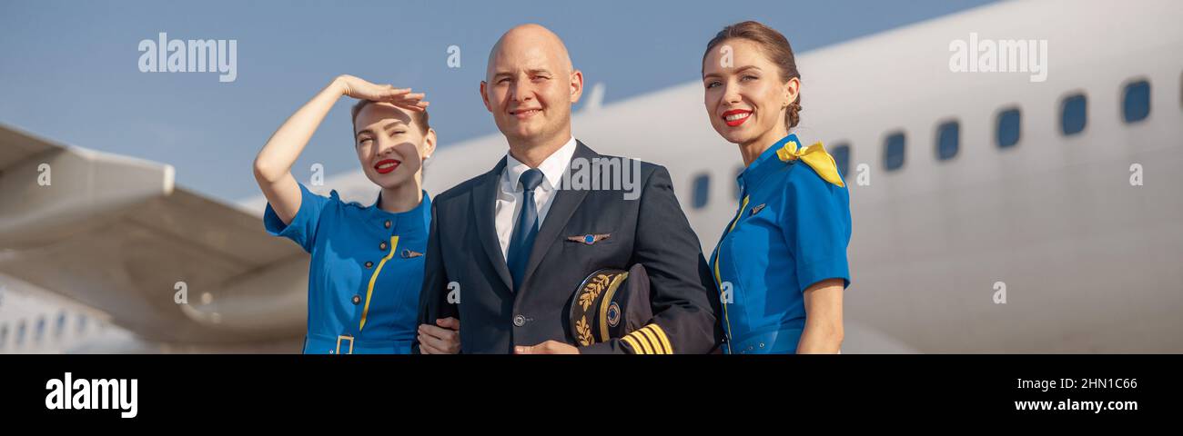 Happy pilot and two attractive stewardesses standing together in front ...