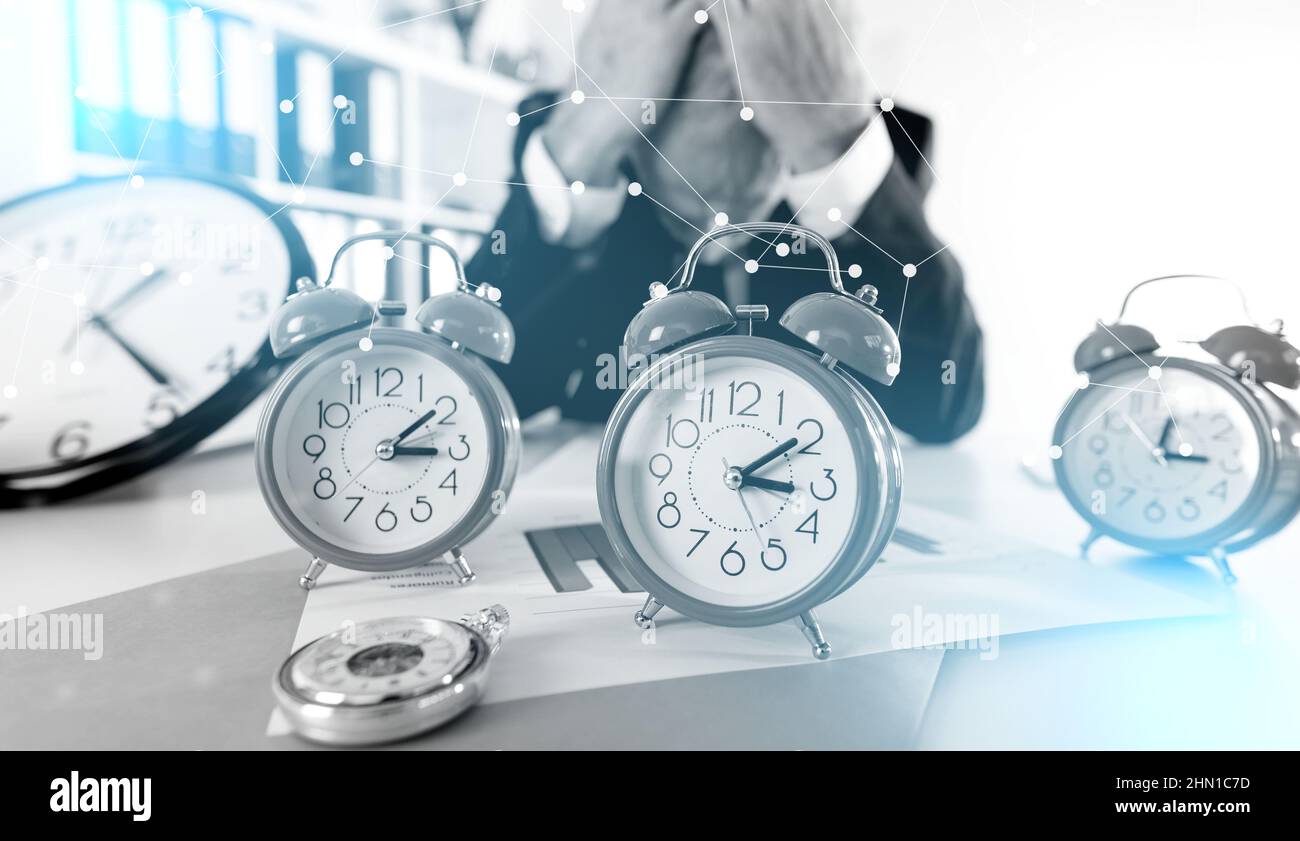 Stressed businessman behind his desk full of alarm clocks Stock Photo ...