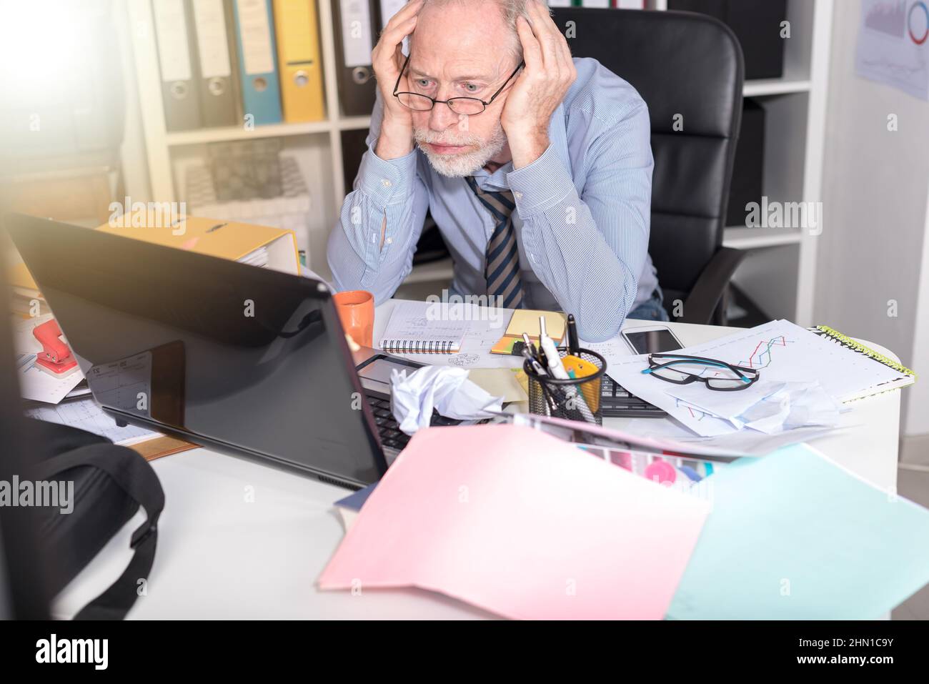 Overworked businessman sitting at a messy desk in office, light effect ...