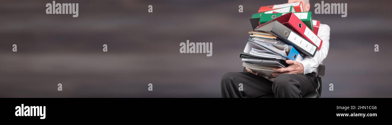 Businessman overworked carrying a pile of binders and folders on grey ...