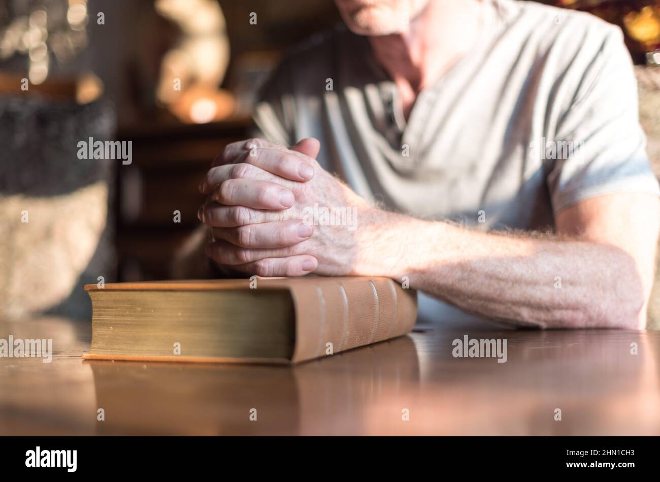 Man sitting at a table praying hands on a Bible Stock Photo - Alamy