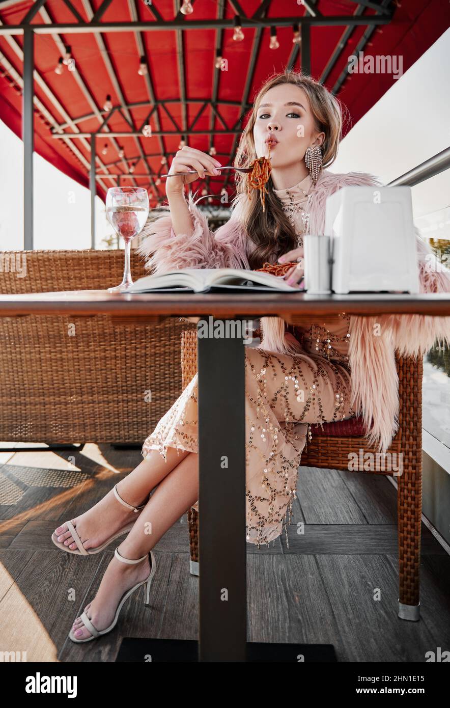 Attractive girl sitting in cafe, eating pasta (spaghetti) and reading a ...