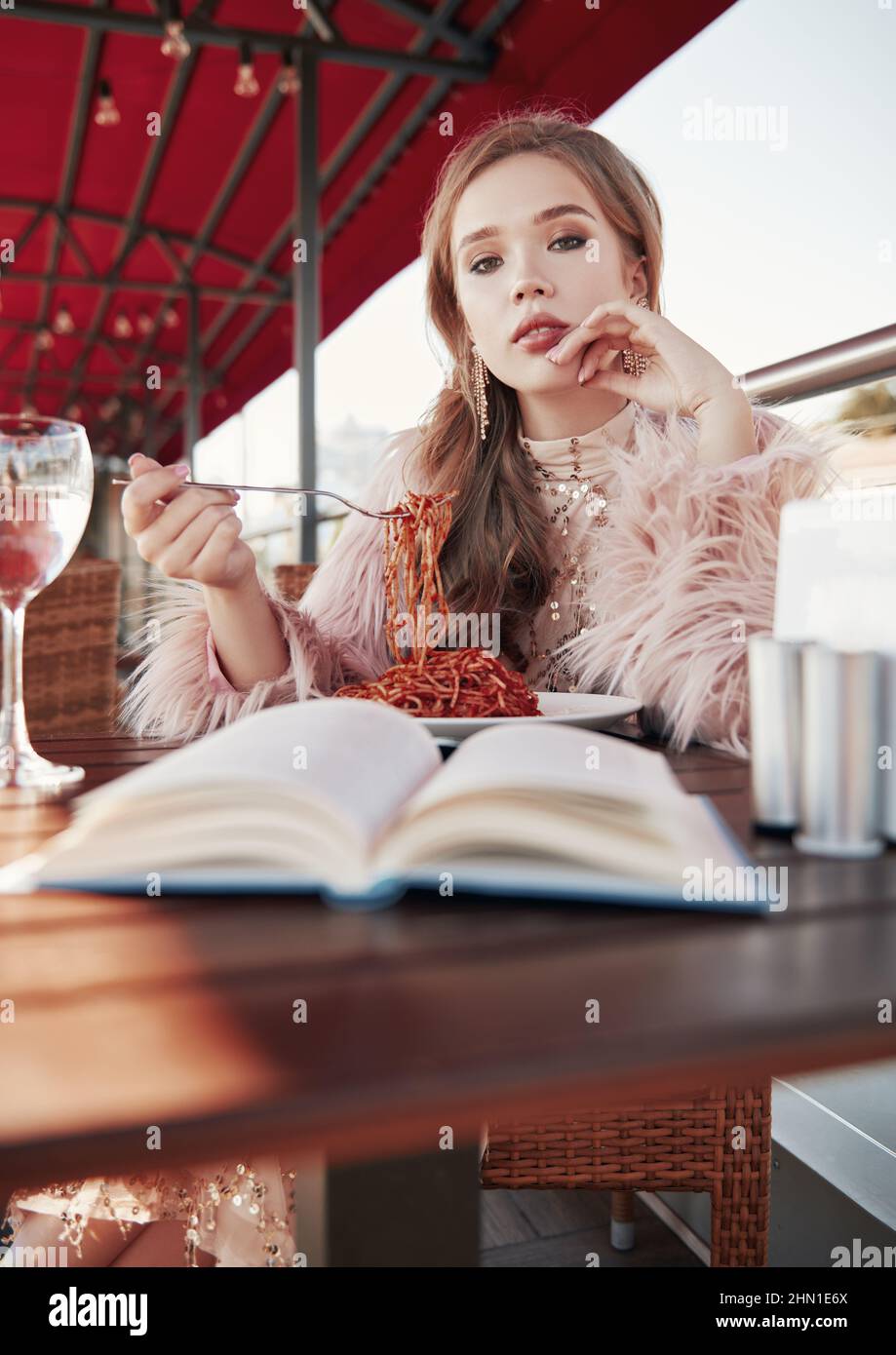 Beautiful girl sitting in cafe, eating pasta (spaghetti) and reading a ...