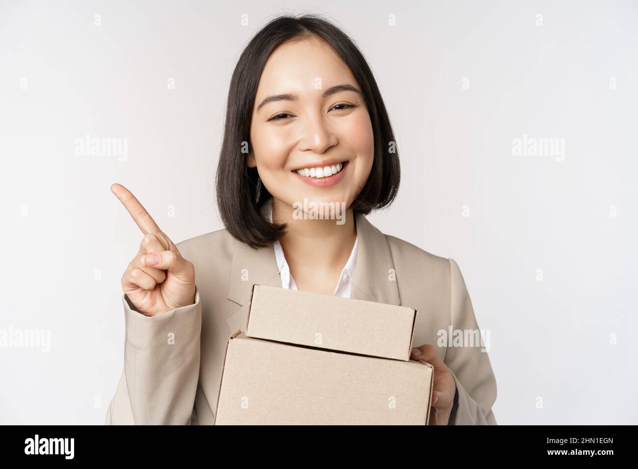 Smiling asian saleswoman pointing finger at copy space, holding boxes ...