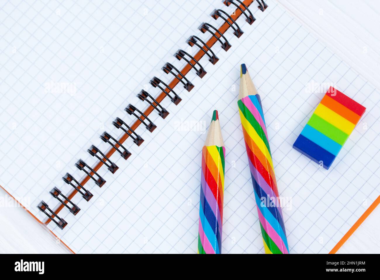 Open copybook with two rainbow-coloured pencils and a rubber on white ...