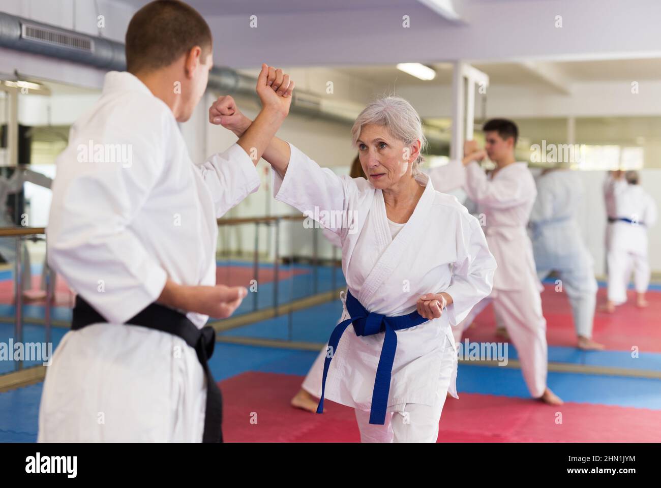 Portrait of woman wearing white kimono sparring with male opponent during martial arts training ...