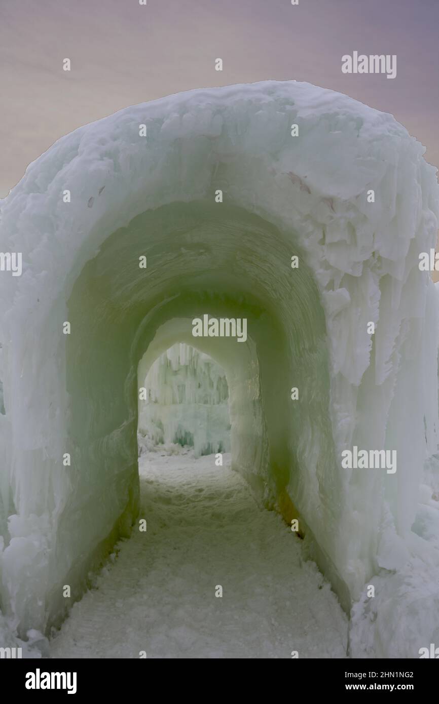 An ice tunnel carved out of ice above a walking path covered in snow at ...