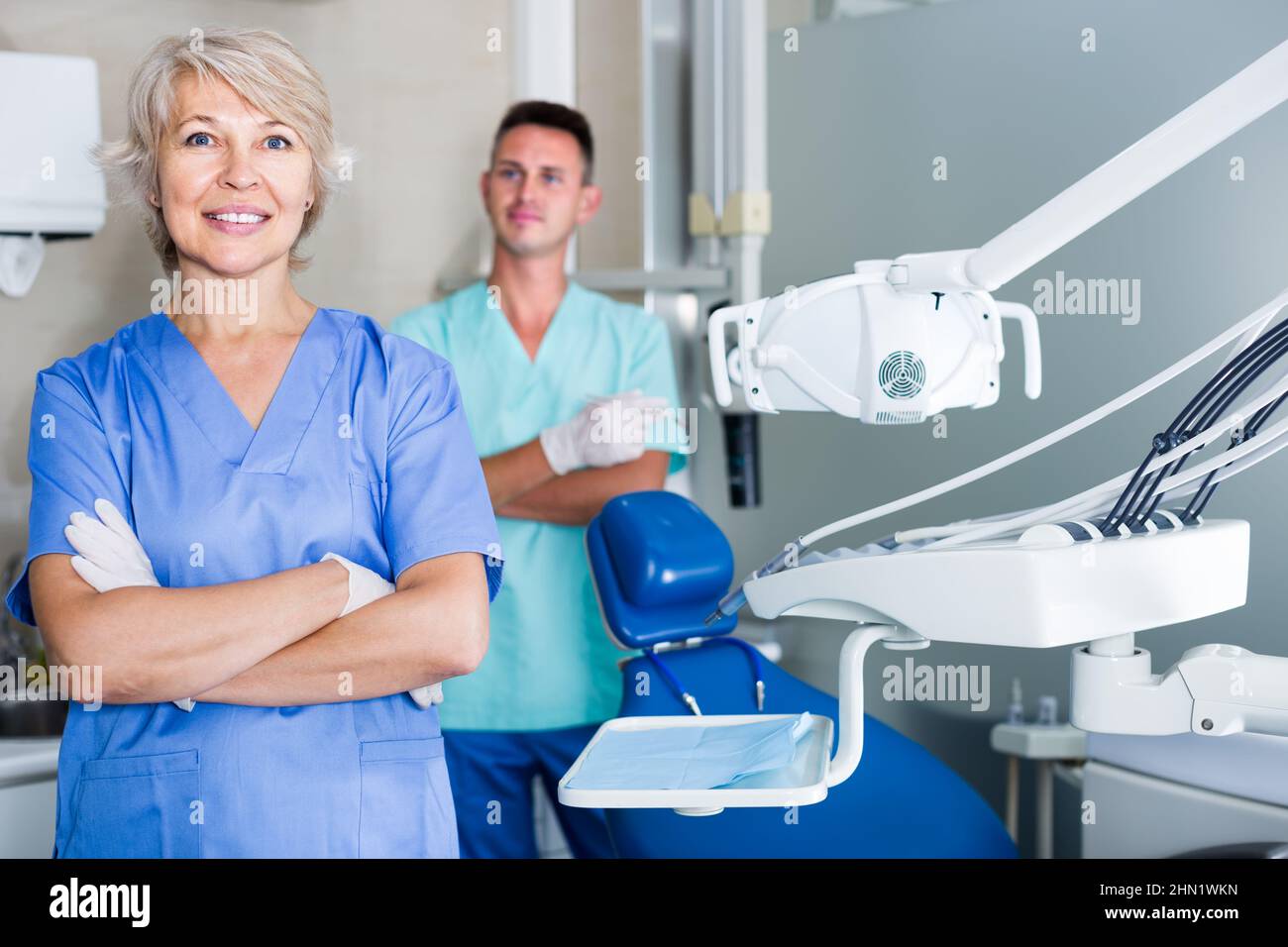 Portrait of friendly woman dentist arms crossed with dental assistant ...