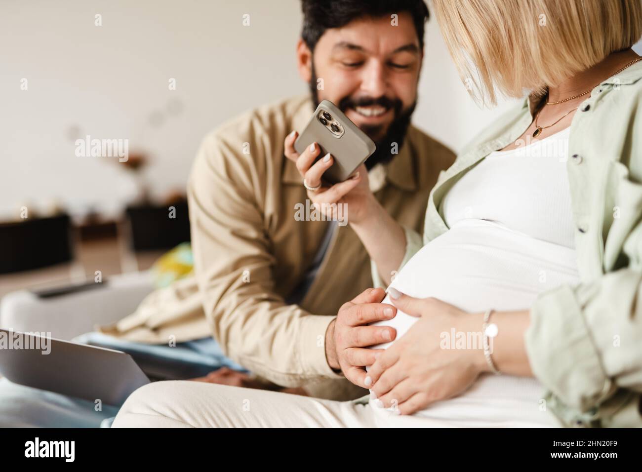 White man touching his pregnant wife's belly while sitting on couch at ...