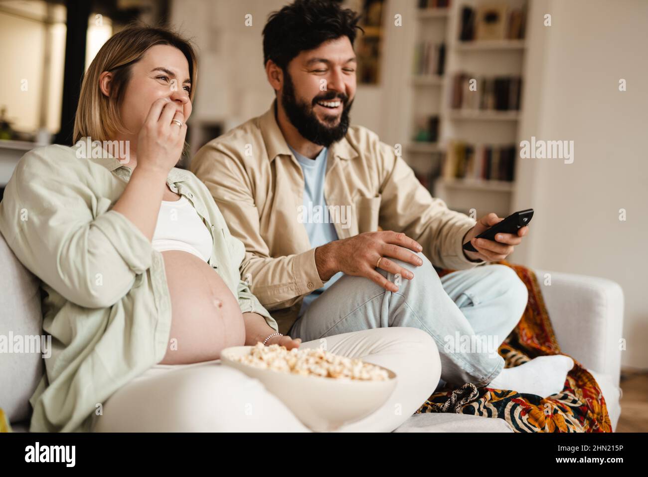 White couple eating popcorn and watching movie while sitting on couch ...