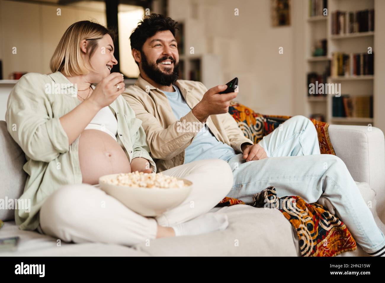 White couple eating popcorn and watching movie while sitting on couch ...