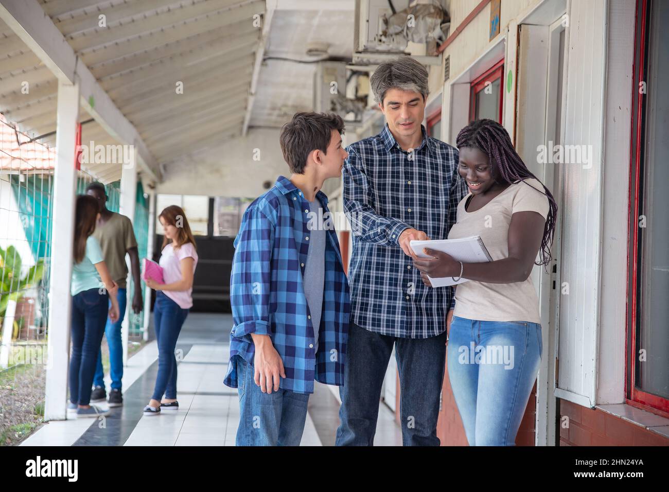 Hight school students talking with their teacher in the hallway, other ...