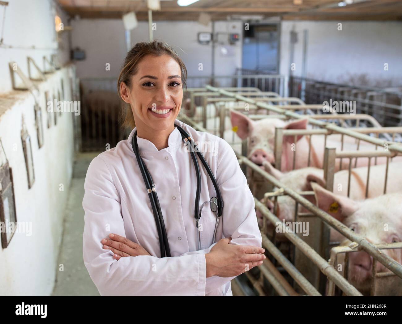 Pretty young veterinarian in white coat with stethoscope standing with ...