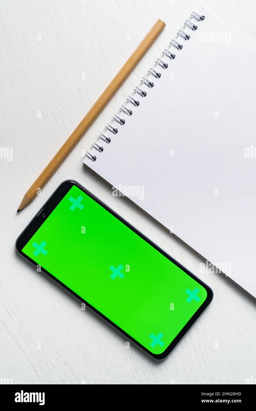White blank notepad smartphone green screen mockup and pencil flat lay ...