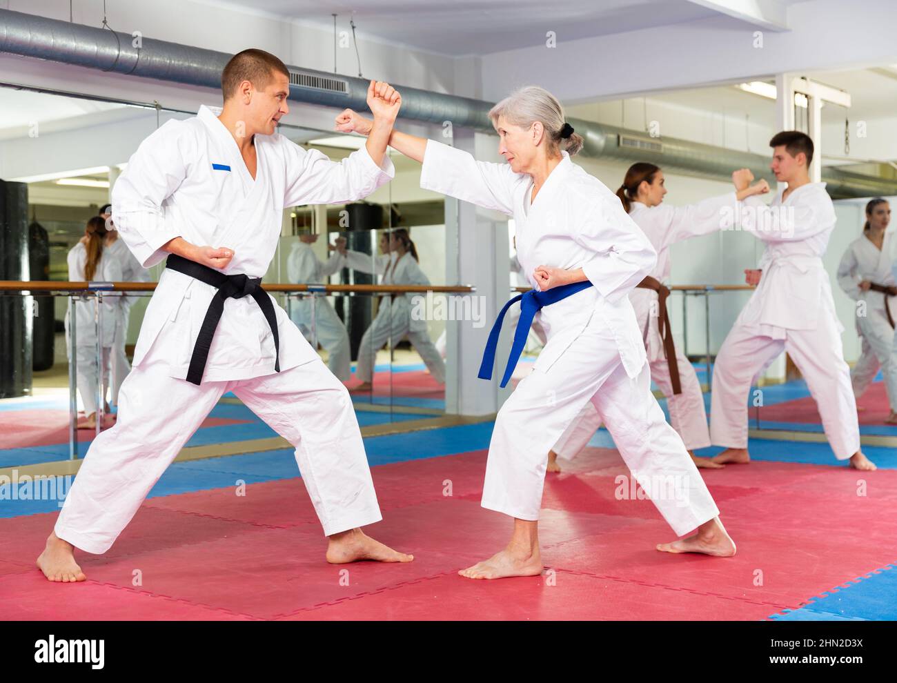Portrait of woman wearing white kimono sparring with male opponent during martial arts training ...