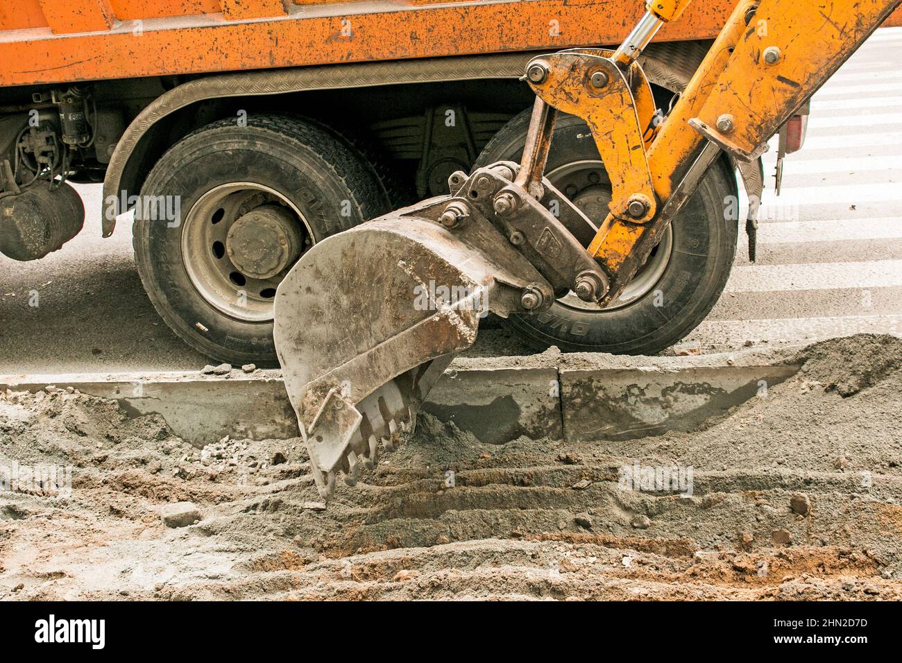 Road works on the city street. The excavator bucket collects the old ...