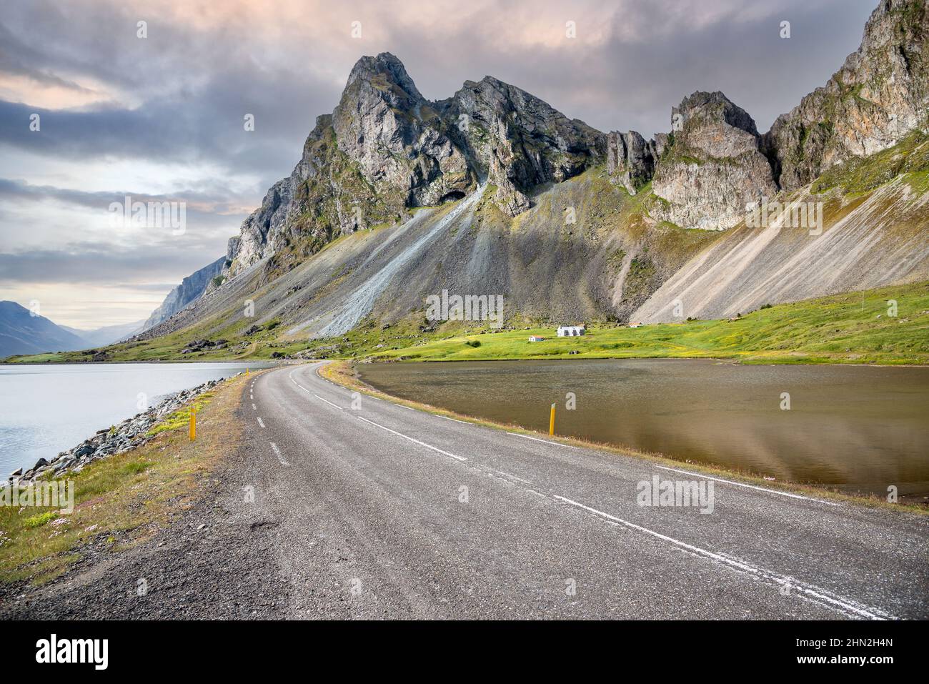 Empty coast road running a the foot of towering mountains at sunset ...