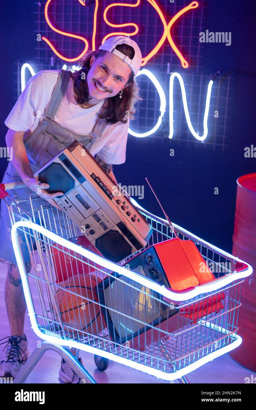 Millennial man with a shopping cart in old retro store buy a tape ...