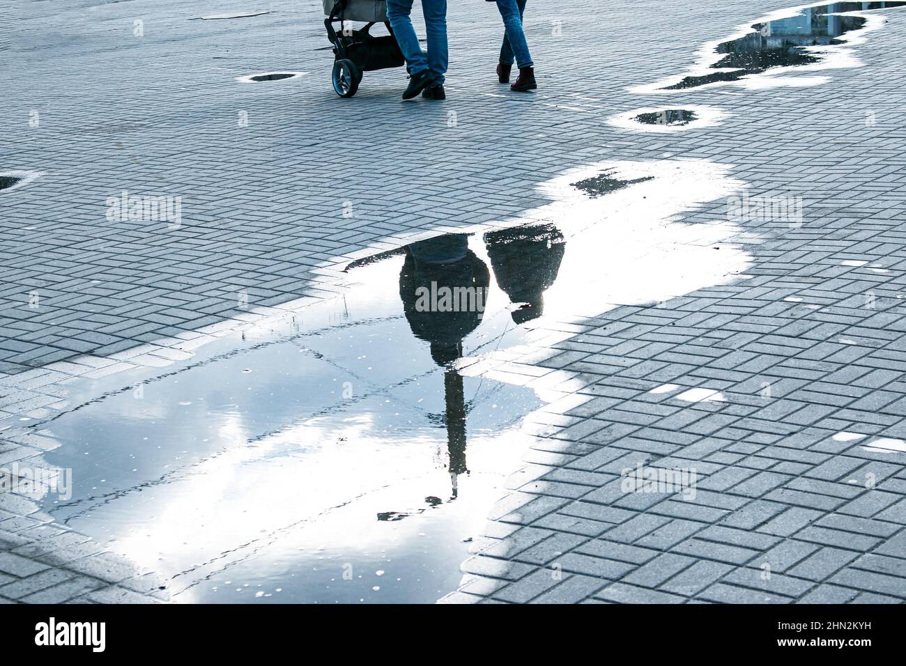 People walking in the park are reflected in a puddle after the rain ...
