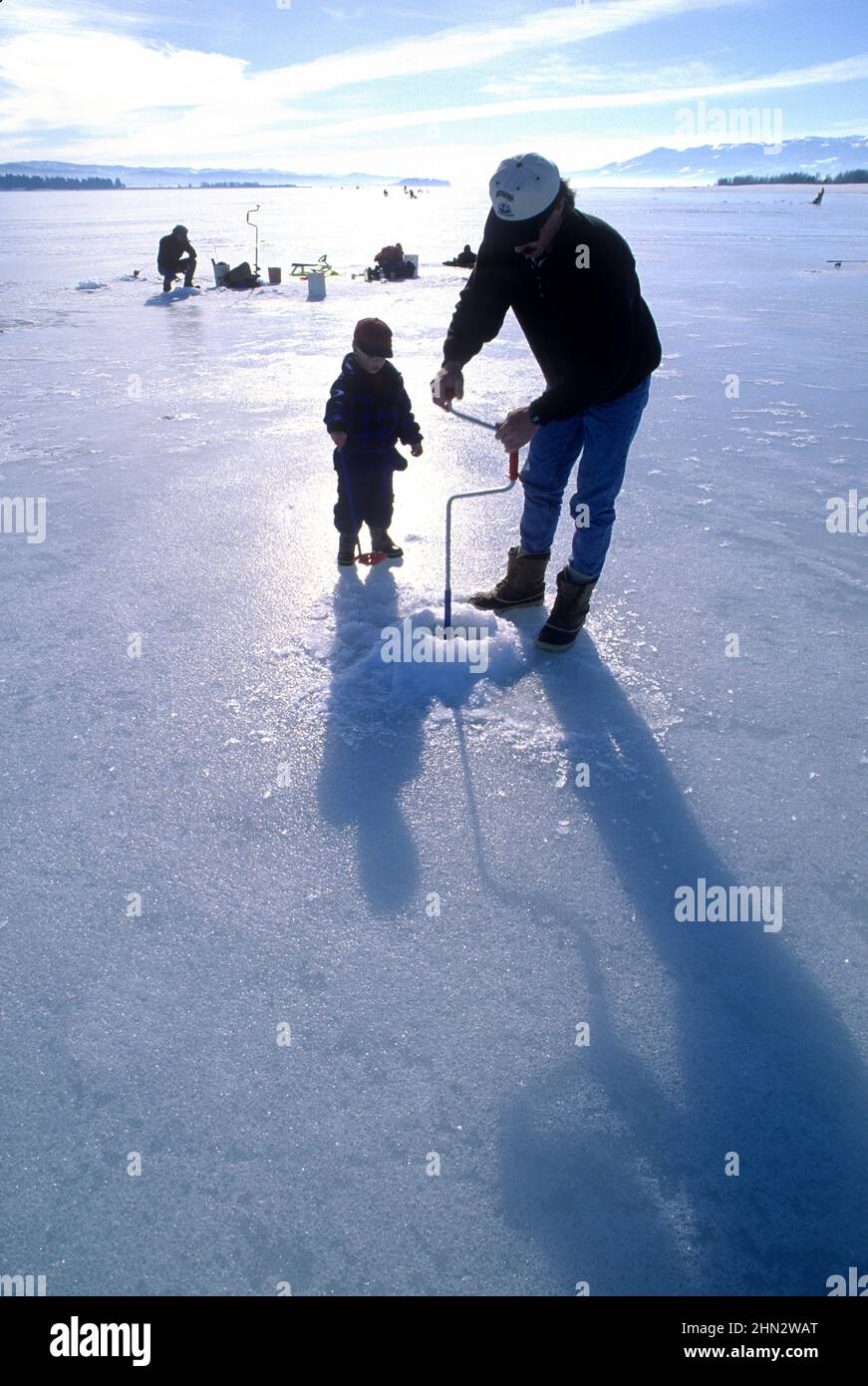 Man and 3-year-old boy drilling hole in ice for ice fishing at Cascade ...