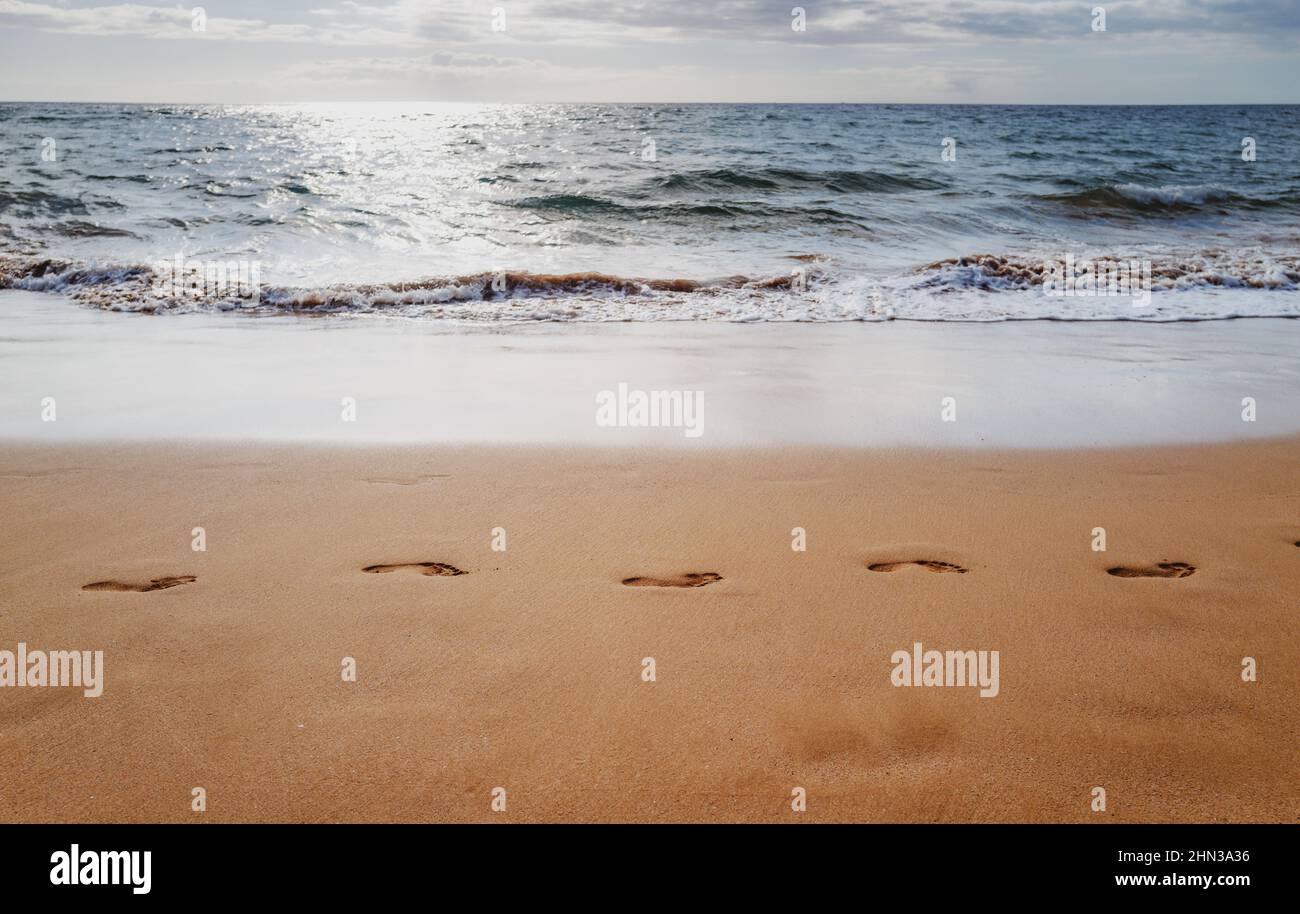 Footprints in the sand at sunset. Sandy tropical beach with sea waves ...