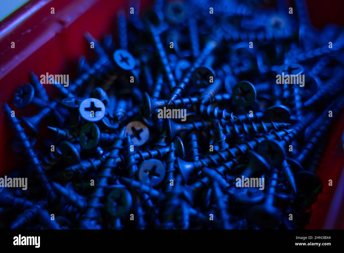 Many black self-tapping screws in a red container under blue light ...