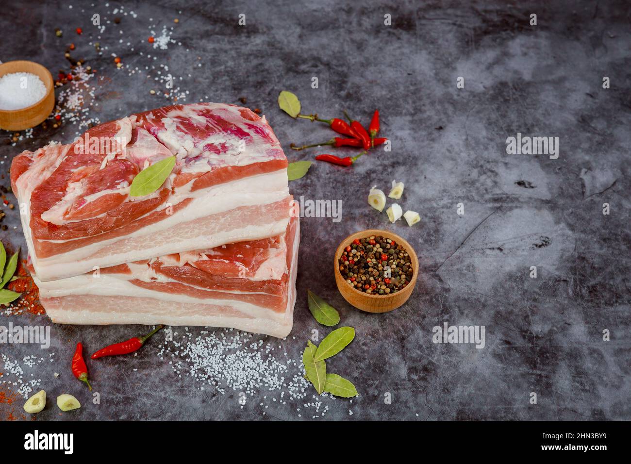 Fresh raw pork belly pieces on dark background with spices and herbs ...