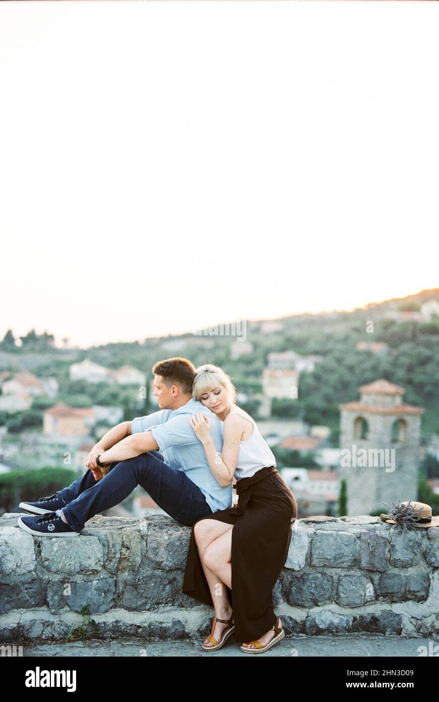 Woman hugs man from behind, resting her head on his shoulder, sitting ...