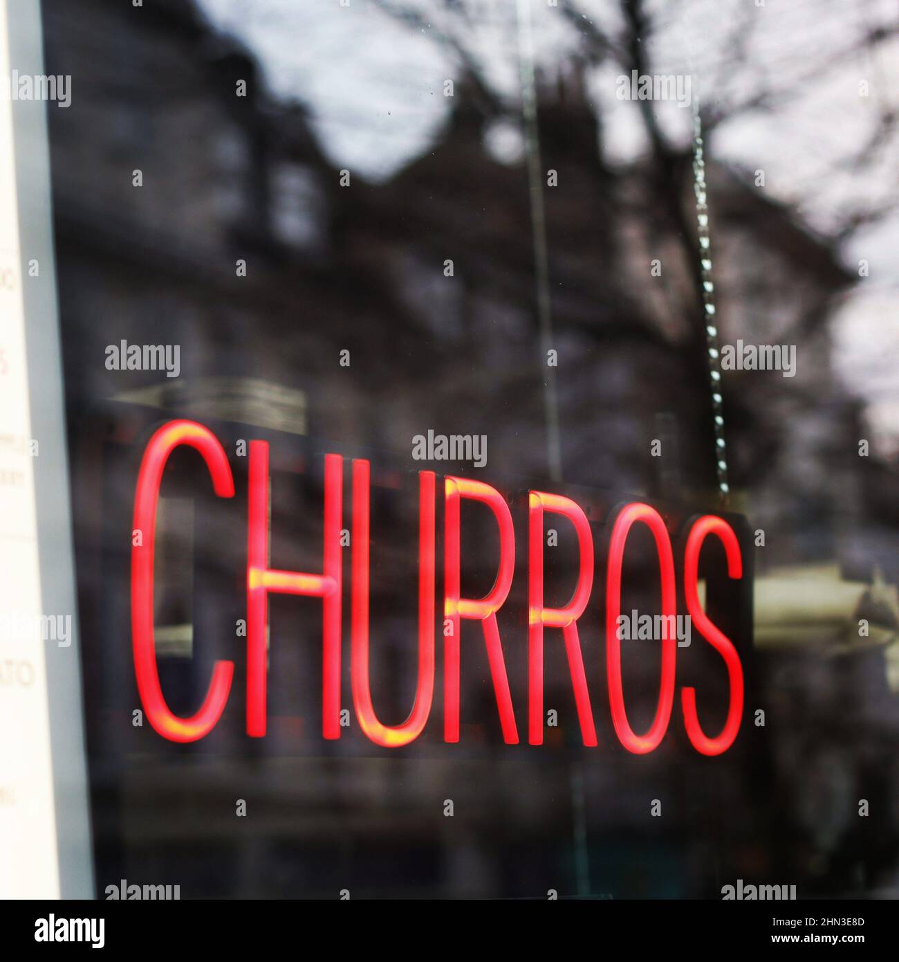 Closeup of a glowing red "churros" sign on a window of a cafe with a ...