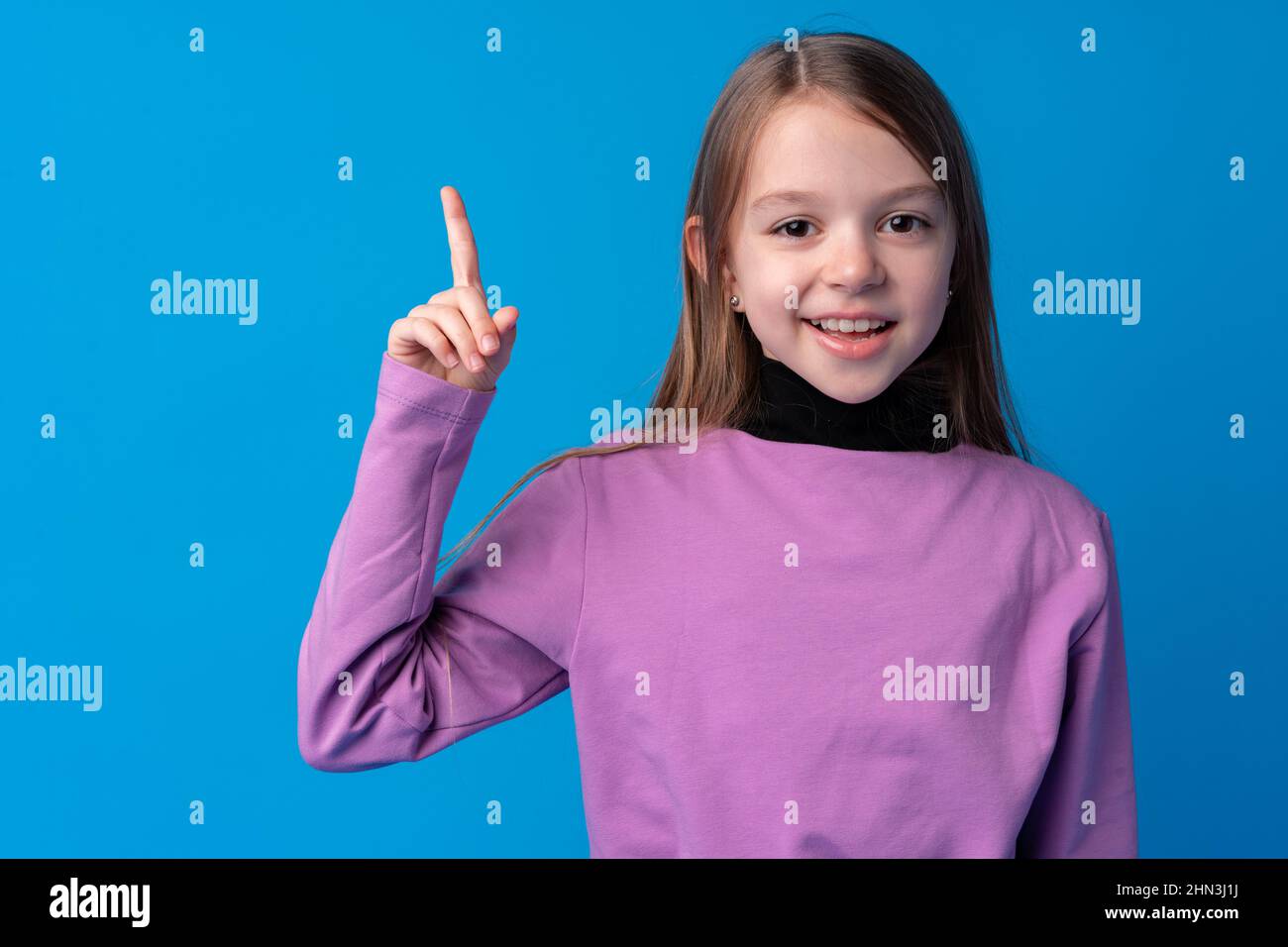 Cute little girl pointing up and having idea against blue background ...