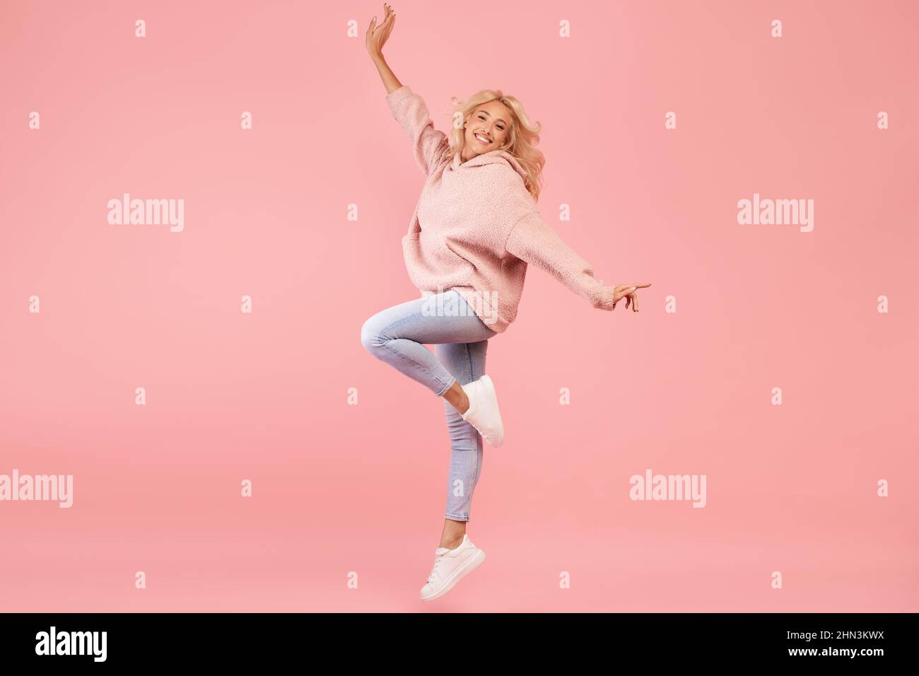 Playful caucasian woman jumping and having fun over pink studio ...