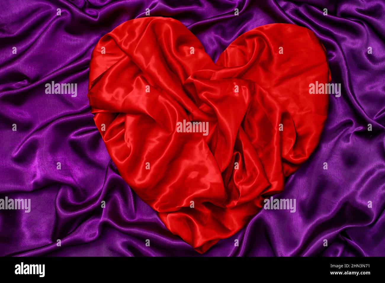 red satin folded as a heart on top of purple satin background ...